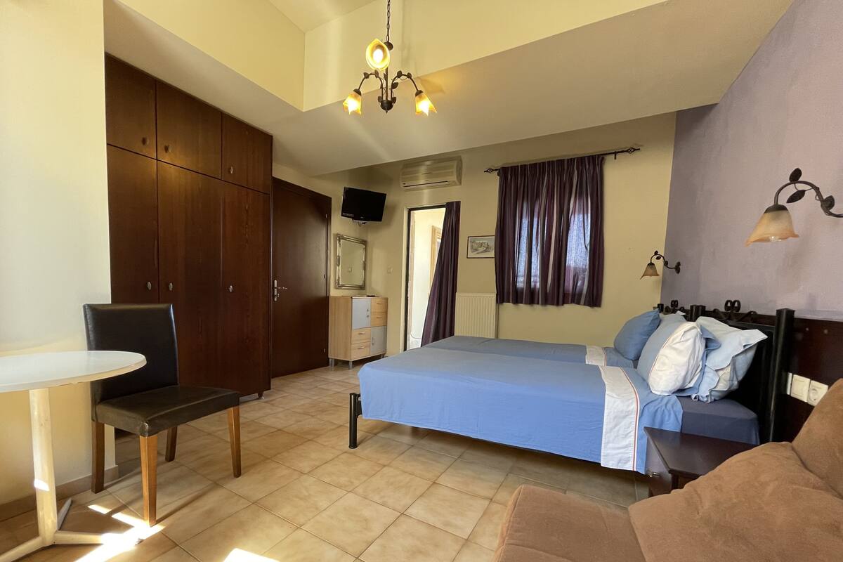 Quarto com cama, escrivaninha, cadeira, guarda-roupa e televisão.