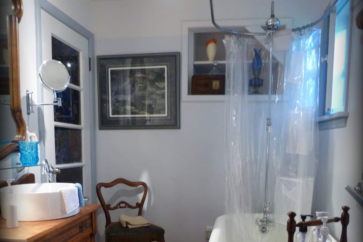 Casa de banho com toucador de madeira, banheira branca, cadeira de madeira e cortina de chuveiro.