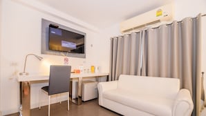 Uma sala de estar moderna com um sofá branco, uma escrivaninha com cadeira, uma televisão de tela plana e um aparelho de ar condicionado.