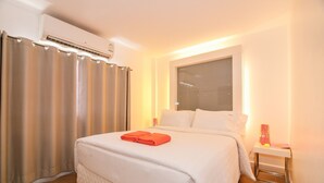 Quarto de hotel com cama, cortinas, mesa de cabeceira e aparelho de ar condicionado.
