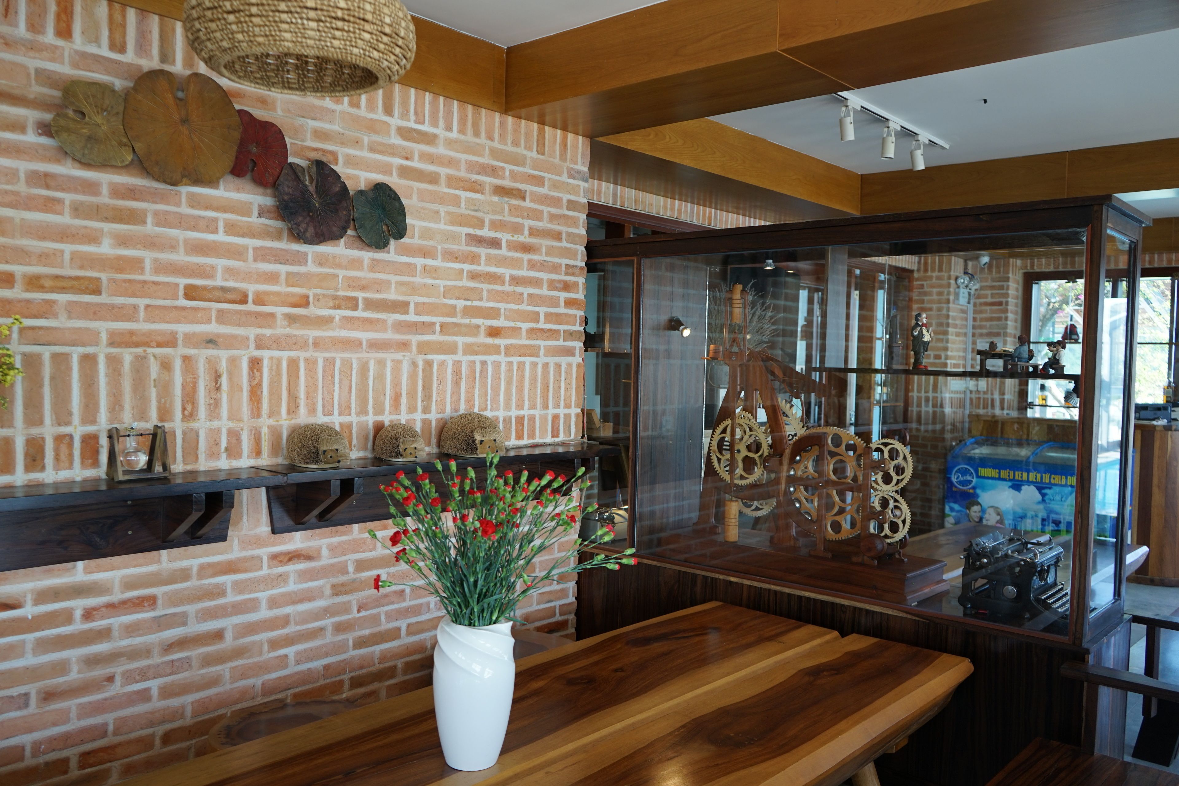 Paredes de tijolo com prateleiras exibindo objetos decorativos e um vaso com flores.