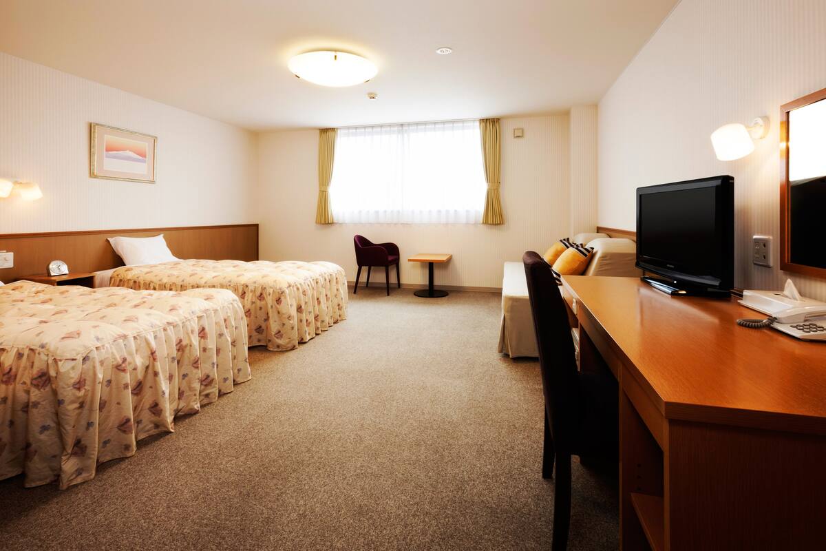 Quarto de hotel com duas camas, uma secretária com televisão e uma mesinha.