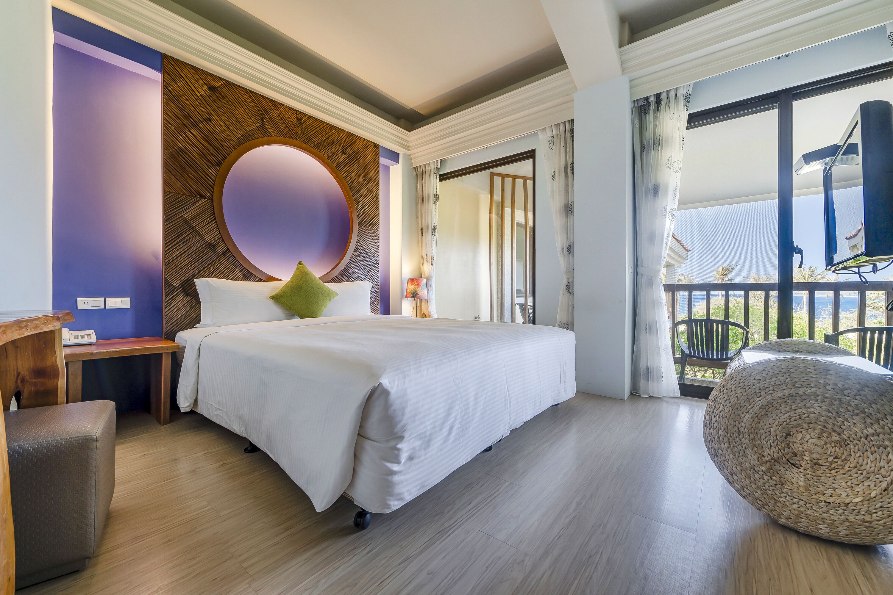 Quarto de hotel moderno com cama grande, escrivaninha e varanda com área de estar externa.