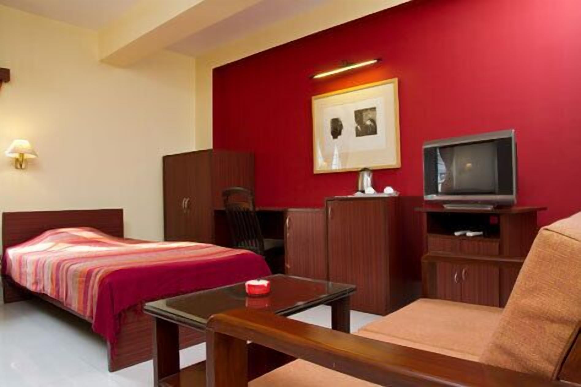 Quarto de hotel com cama, escrivaninha, cadeira, televisão e guarda-roupa.