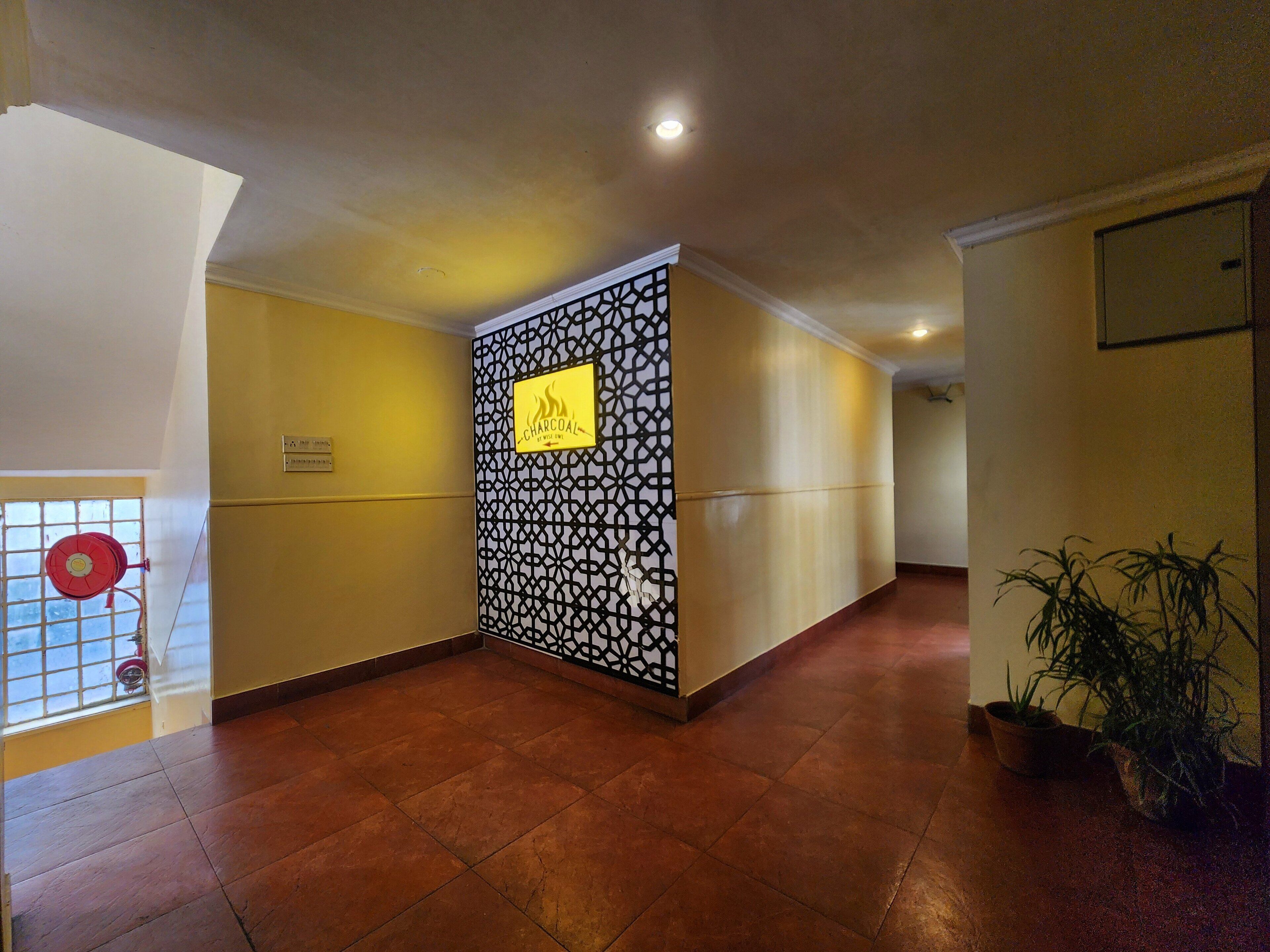 Um corredor com papel de parede estampado, uma placa com a palavra "Charcoal" e um vaso de planta.