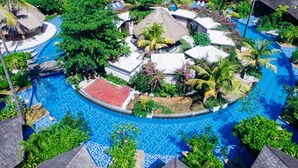 Um resort com uma piscina central cercada por vegetação exuberante e construções com telhados de palha.