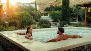 Um casal relaxando em uma banheira de hidromassagem, com vista para um jardim paisagístico e uma montanha ao fundo.