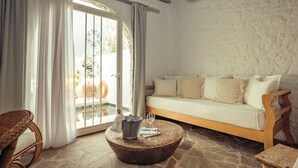 Um quarto acolhedor com piso de pedra, uma cadeira de vime, um sofá de madeira e uma mesa de centro redonda com uma garrafa e um copo.
