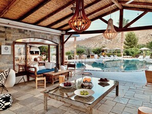 Área à beira da piscina com mesa de vidro, assentos e vista para a piscina.
