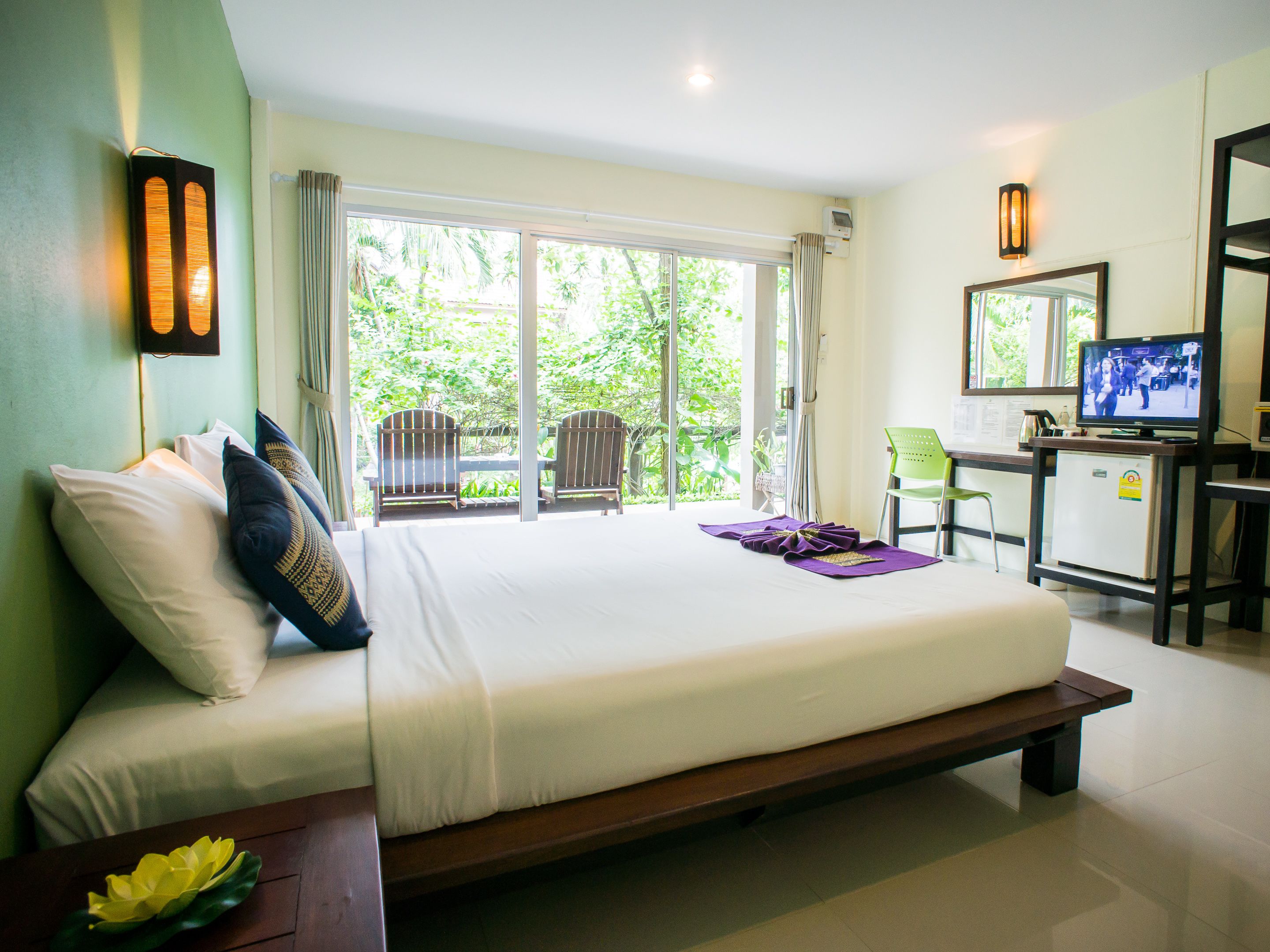 Quarto de hotel com uma cama, uma escrivaninha com computador, uma cadeira e vista para o verde lá fora.