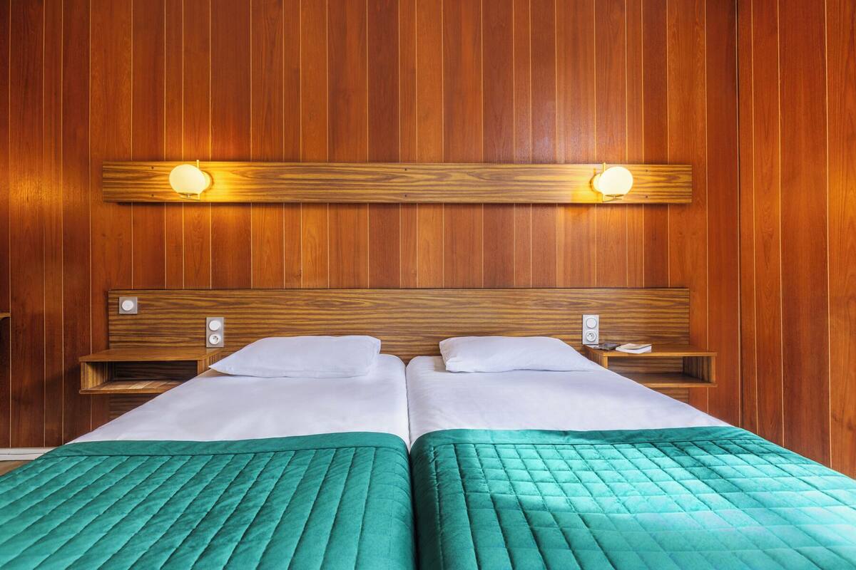 Uma cama de casal com cabeceira de madeira e duas mesas de cabeceira, cada uma com uma luminária.