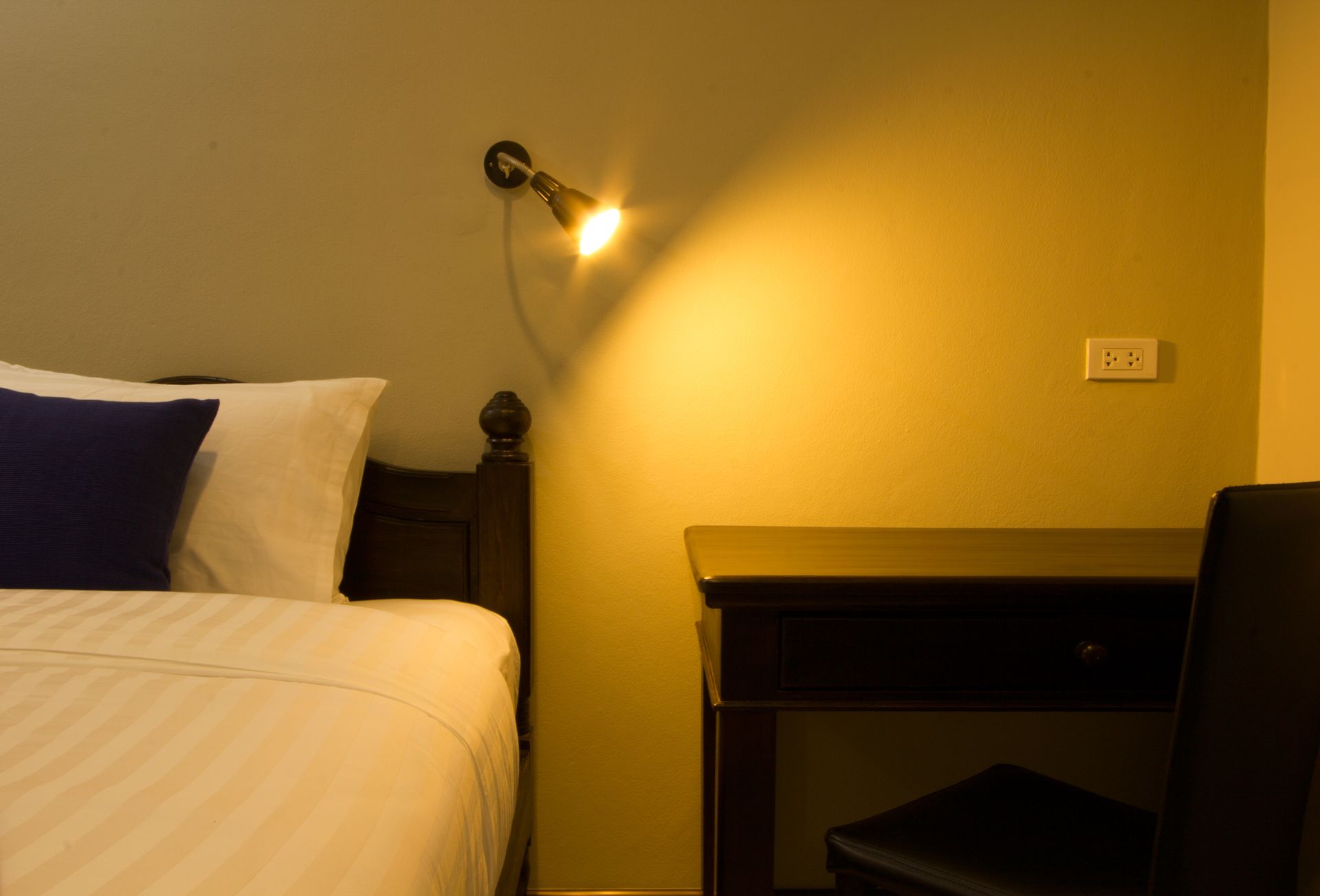 Quarto de hotel com cama, mesa de cabeceira e luminária.