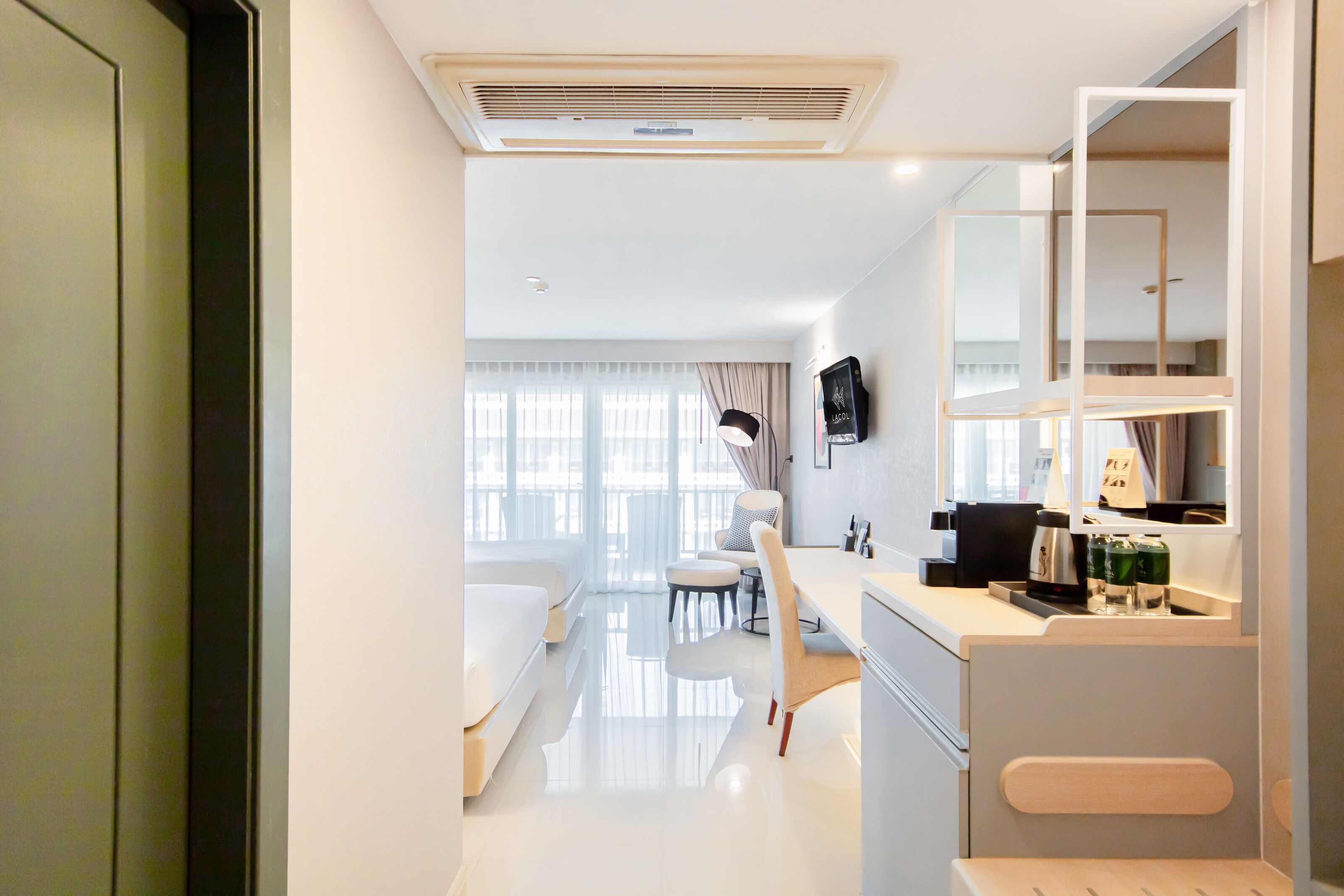 Quarto de hotel moderno com cama, escrivaninha, cadeira, televisão e minibar.