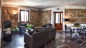 Uma sala de estar com parede de pedra, um sofá, uma mesa de centro e uma televisão.