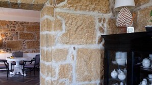 Quarto com parede de pedra, área de jantar com mesa e cadeiras, e armário com louças brancas.