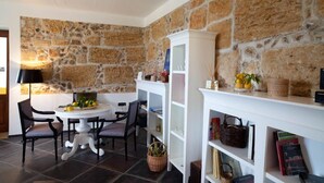 Uma área de refeições com parede de pedra, uma mesa redonda com cadeiras e um armário branco com prateleiras.
