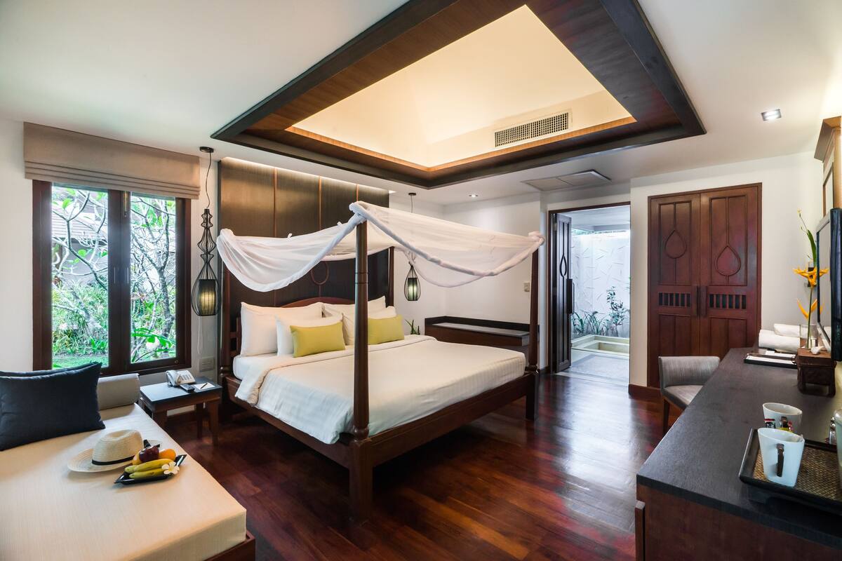 Um quarto espaçoso com uma cama de dossel, uma escrivaninha com cadeira e vista para o exterior através de amplas janelas.