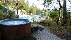 Uma banheira de hidromassagem numa varanda de madeira, com uma piscina ao fundo.