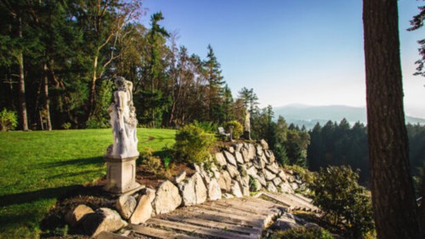 Uma trilha de pedra leva a uma estátua em um parque, com vista para montanhas ao longe.