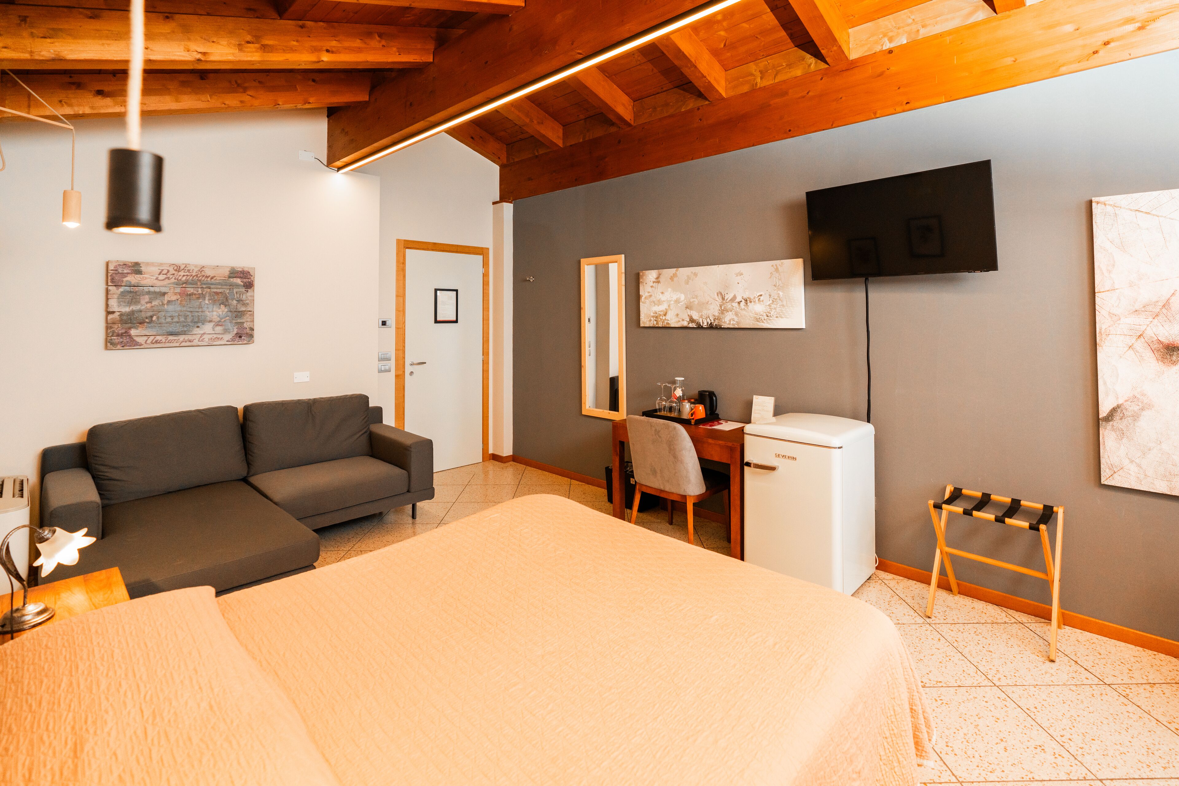 Quarto de hotel moderno com cama, sofá, escrivaninha, televisão e obras de arte nas paredes.