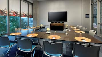 Uma sala de conferências com uma mesa comprida, cadeiras, uma TV de tela plana e vista para árvores através de grandes janelas.