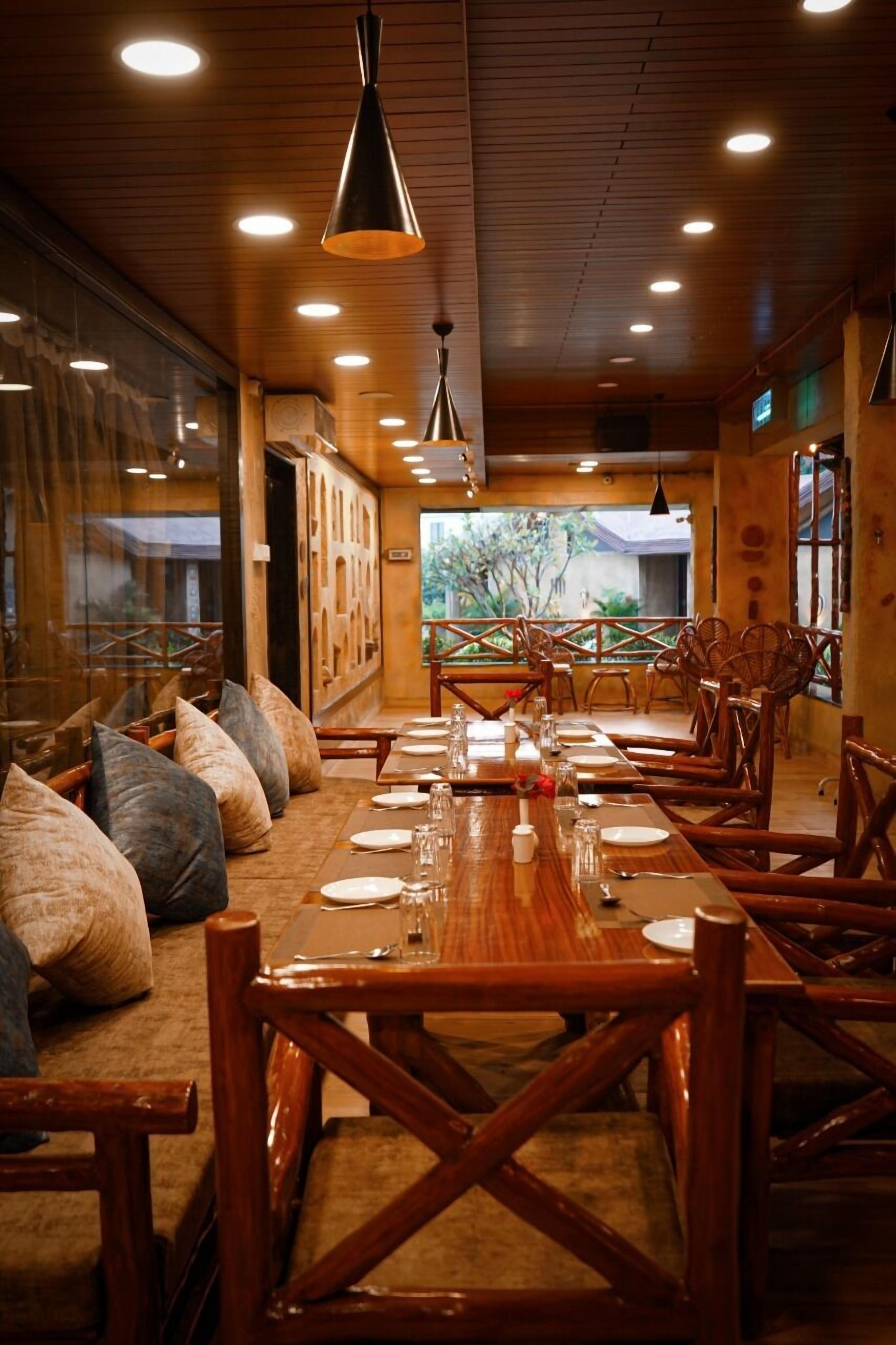 Um restaurante com uma longa mesa de madeira preparada para refeições, rodeado por cadeiras de vime.