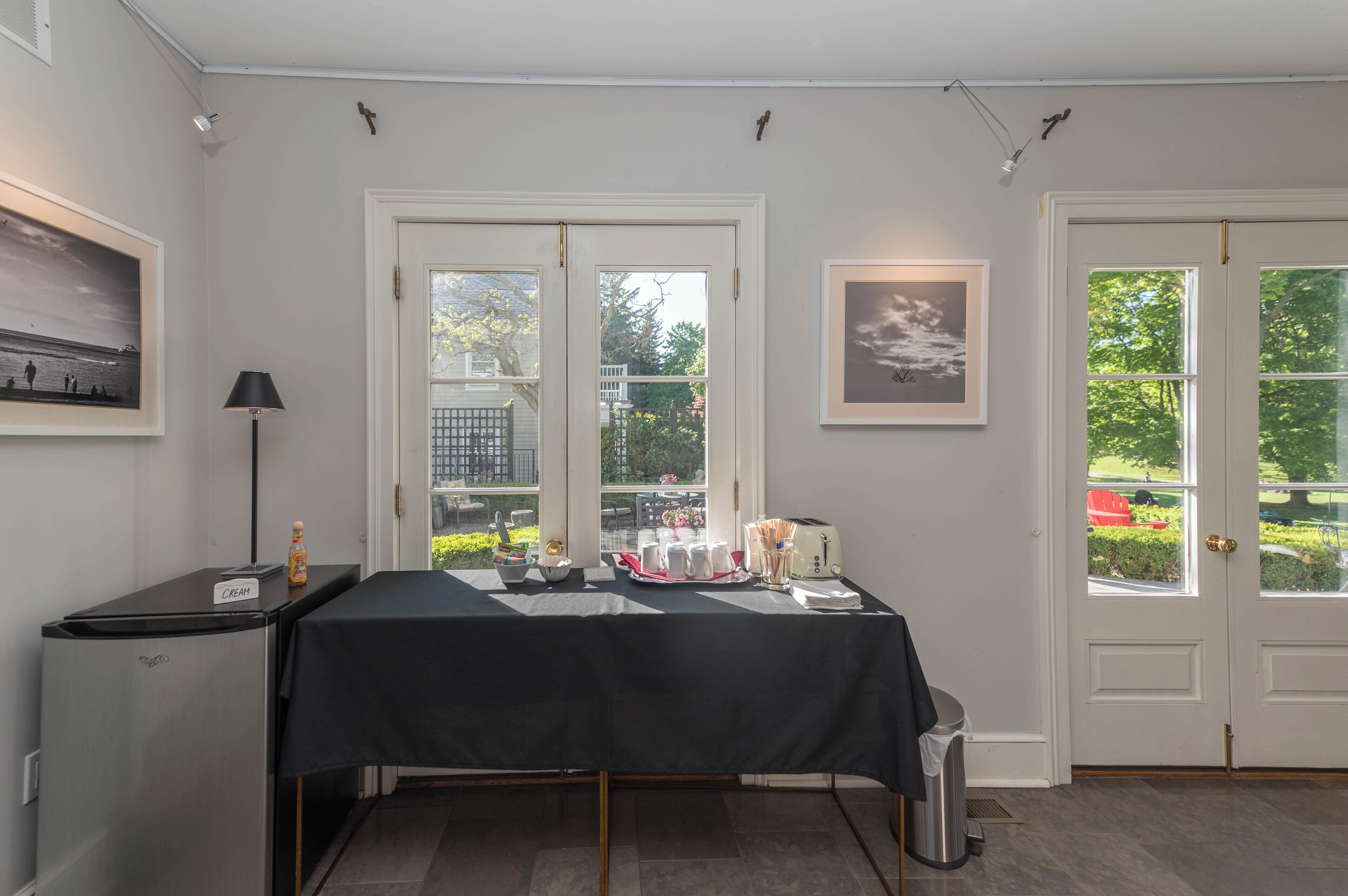Quarto com mesa posta para refeição, geladeira e duas portas com janelas.