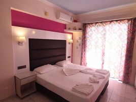 Quarto com uma cama grande, mesas de cabeceira, ar condicionado fixado na parede e uma janela com cortinas estampadas.
