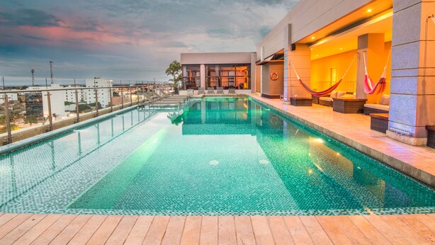 Uma piscina infinita no terraço com vista para o horizonte da cidade, uma área de estar com assentos e um edifício moderno com grandes janelas.