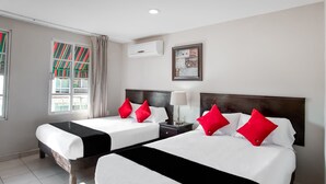 Quarto de hotel com duas camas, janela com cortinas listradas, ar condicionado, mesa de cabeceira com abajur e quadro na parede.
