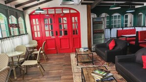 Um ambiente acolhedor com cadeiras de vime, um sofá preto com almofadas vermelhas, uma mesa de centro de madeira e uma porta vermelha com painéis de vidro.