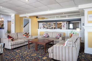 Um hall de hotel com sofás listrados, uma mesa de centro e um espaço de bar com vários frascos.