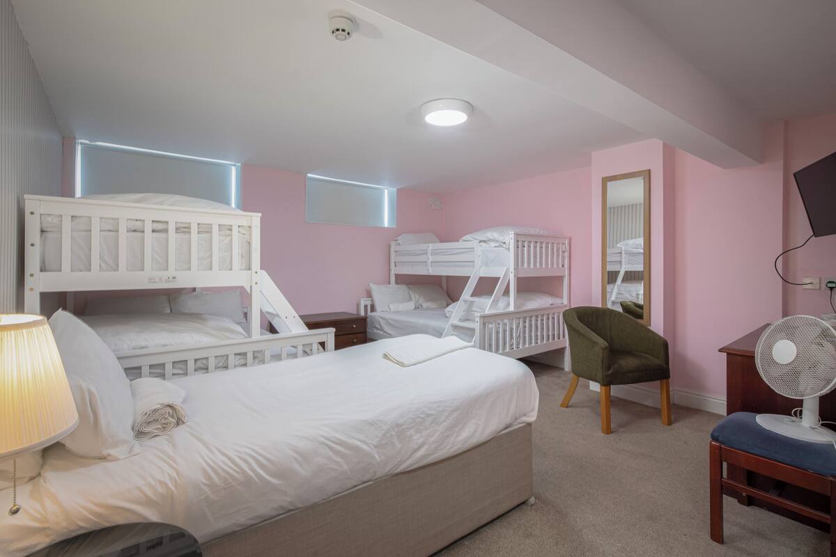 Quarto com beliches, escrivaninha, cadeira, abajur, espelho e ventilador.