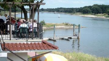Um terraço à beira do lago com pérgola, mesas ao ar livre e vista para o lago.