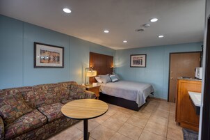 Quarto de hotel com sofá, cama, mesa redonda pequena e armário de madeira.