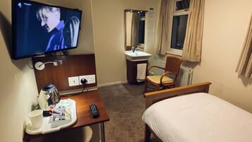 Quarto de hotel com uma cama, uma escrivaninha com cadeira, televisão, pia e janela com cortinas.