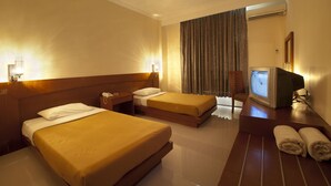 Quarto de hotel com duas camas, televisão, secretária e janela com cortinas.