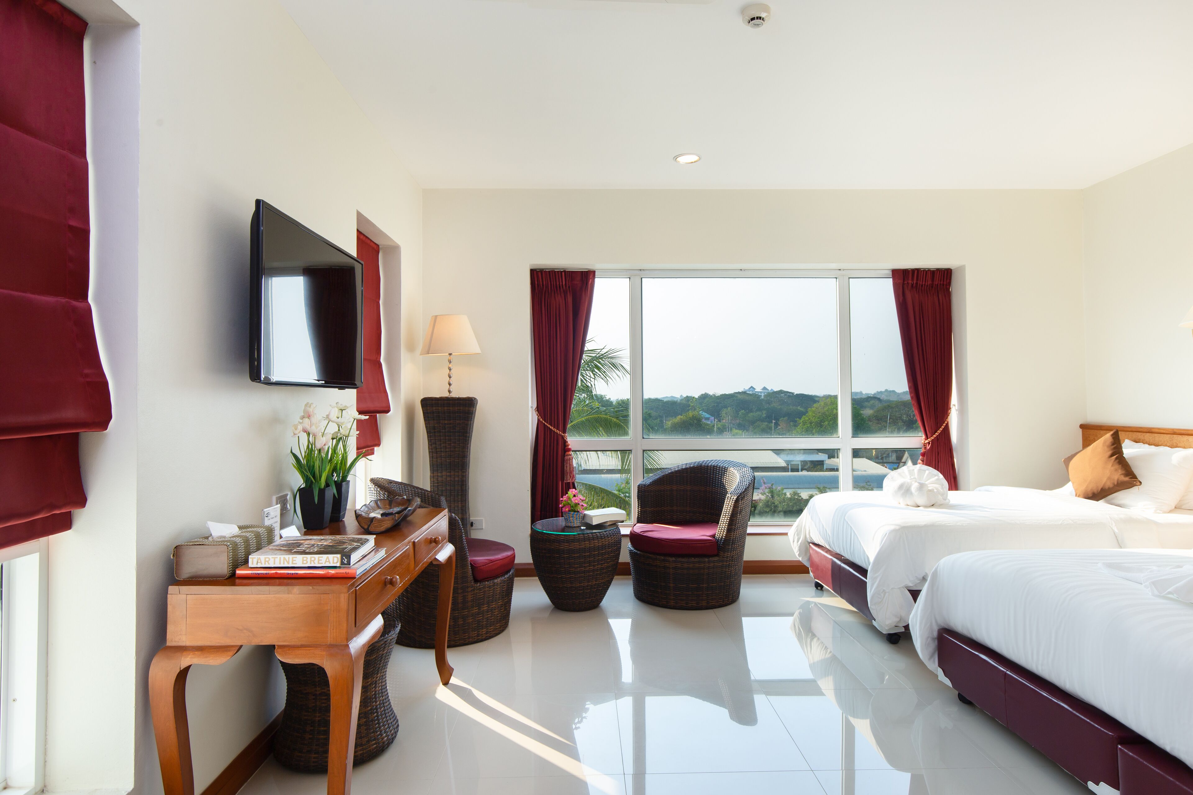 Quarto de hotel com cama, escrivaninha, cadeira, televisão e janela com cortinas.