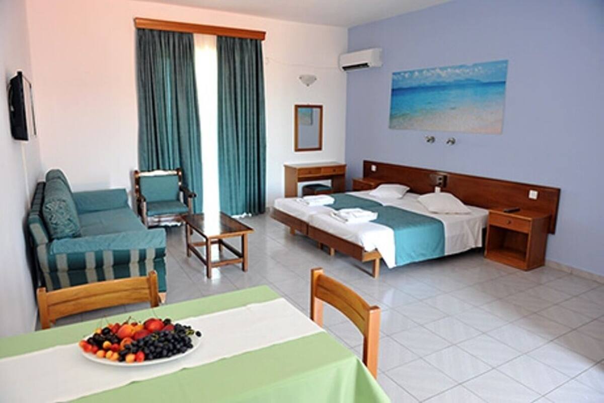 Quarto de hotel com cama, sofá, escrivaninha e mesa de jantar com frutas.