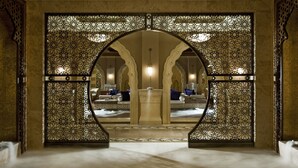 Interior luxuoso com portões metálicos ornamentados, um arco central e um espaço de estar com almofadas.