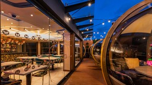 Um interior moderno com parede de vidro curva, piso de madeira e área de bar com prateleiras e iluminação.