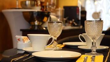 Mesa posta com pratos brancos, um copo transparente, uma xícara branca e um guardanapo amarelo com faca e colher.