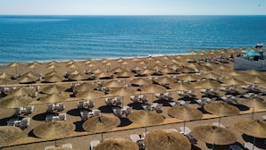 Uma praia com fileiras de espreguiçadeiras e guarda-sóis de palha.