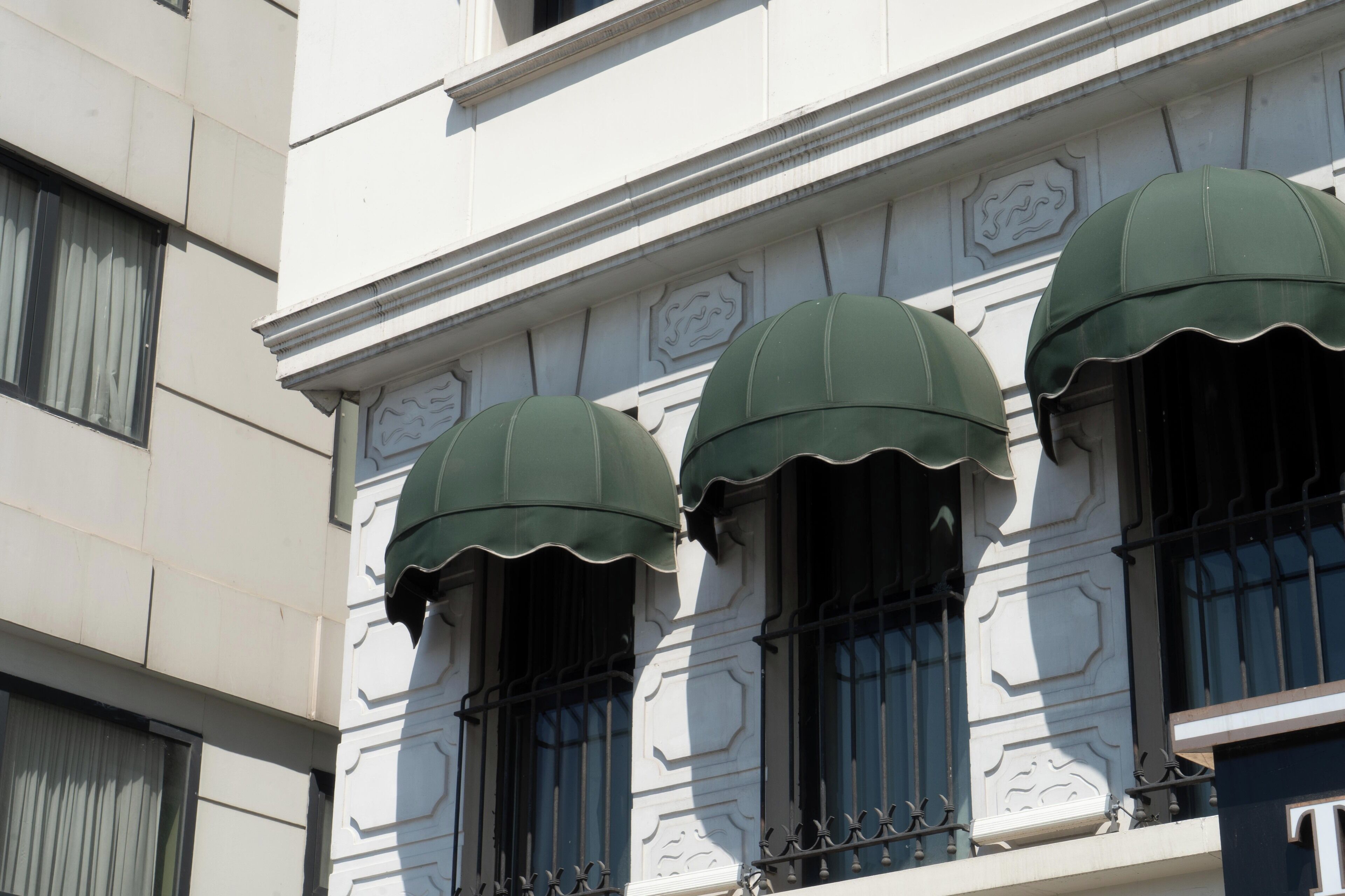 Fachada de edifício com três janelas em arco, cada uma com toldo verde.