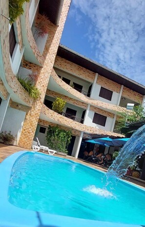Um edifício com vários andares, piscina e um elemento decorativo com água.