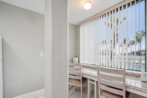 Quarto com mesa de jantar, cadeiras, cafeteira e janela com persianas.