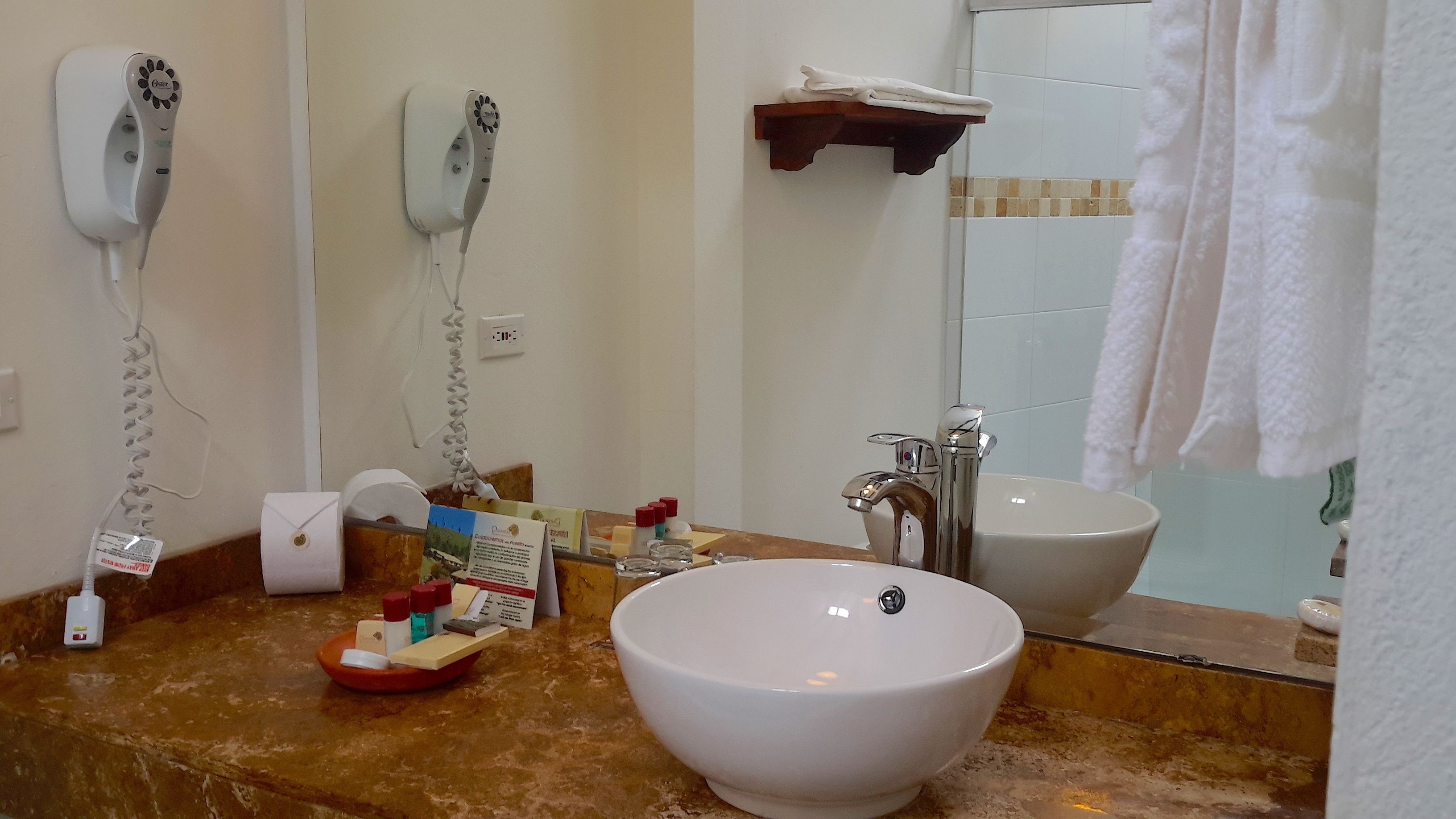Casa de banho com lavatório, espelho, porta-toalhas e secadores de cabelo fixados na parede.