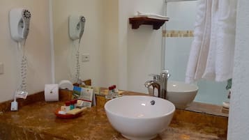 Casa de banho com lavatório, espelho, porta-toalhas e secadores de cabelo fixados na parede.