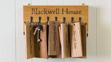 Uma placa de madeira com o nome 'Blackwell House' e um conjunto de ganchos de madeira para chaves abaixo, cada um identificado com nomes de quartos como 'The Orchard Room' e 'The Loft Suite'.