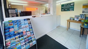 Uma área de recepção de hotel com um letreiro de neon para o Maple Leaf Inn & Suites, uma mesa com um computador e uma exposição de folhetos de viagem.